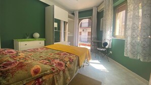 Quarto com cama, penteadeira e varanda com cadeira.
