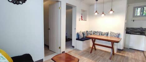 Uma sala de estar com sofá, mesa de centro de madeira, mesa de jantar com bancos e uma área de cozinha com pia e bancada.