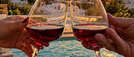Duas mãos segurando copos de vinho com vista do pôr do sol sobre a água.