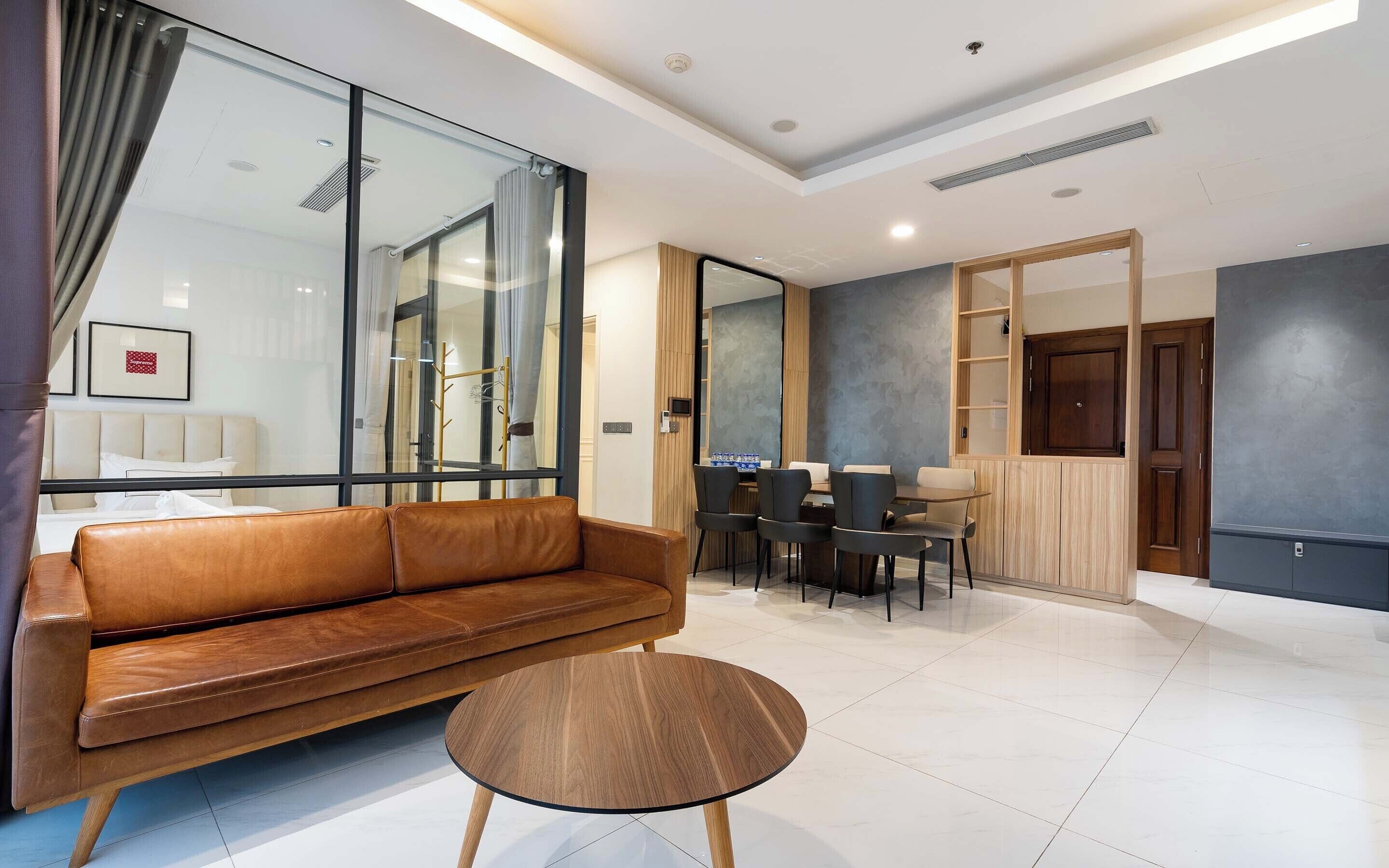 Quarto de hotel moderno com sofá de couro, mesa de centro redonda de madeira e área de refeições com cadeiras e mesa.