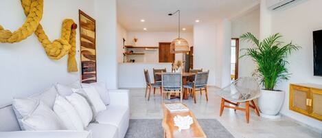 Uma sala de estar moderna com um sofá branco, uma mesa de centro de madeira e um espaço de jantar com mesa e cadeiras.