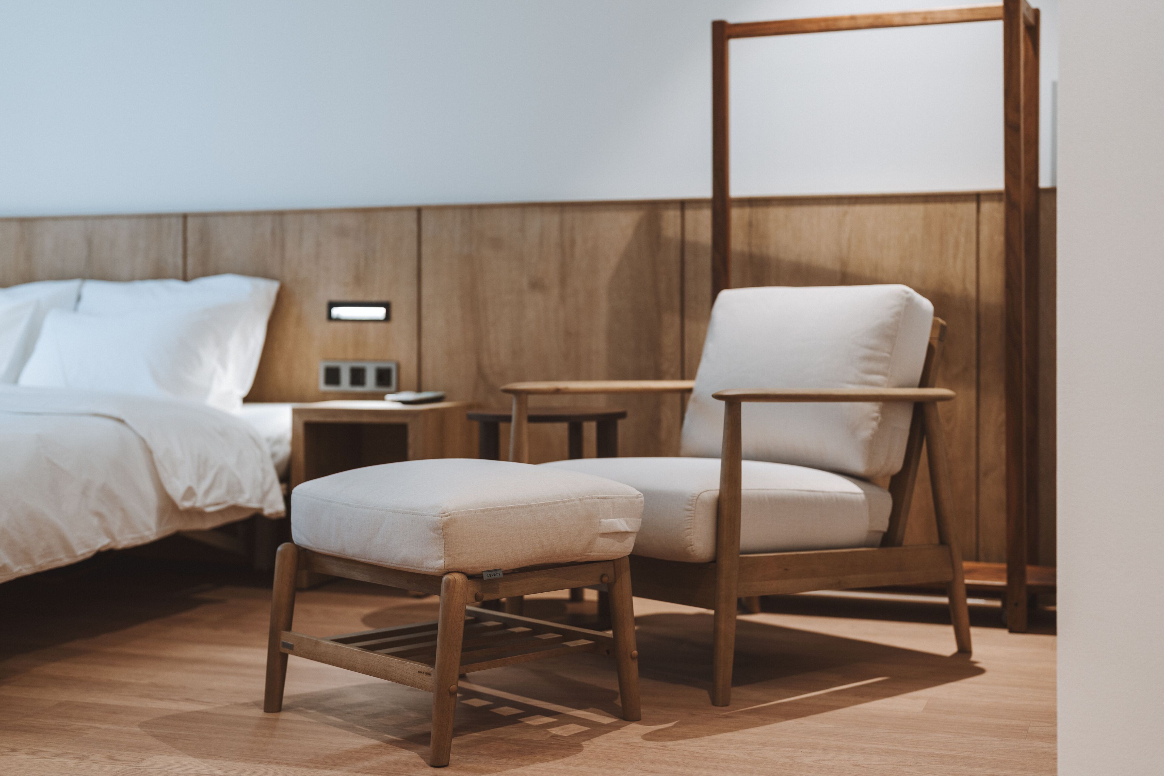 Quarto com cama, duas cadeiras, mesa de cabeceira e cabeceira de madeira.