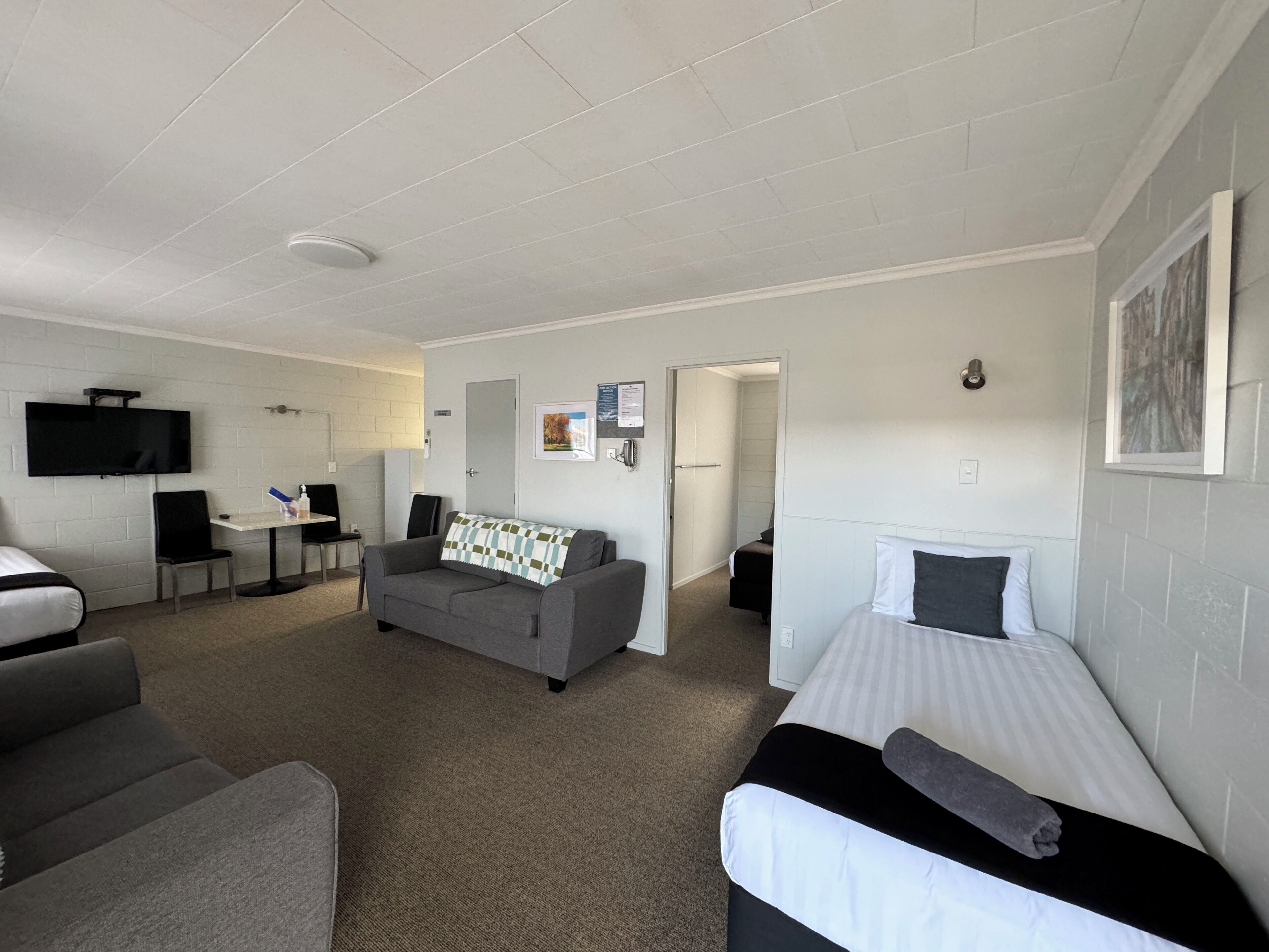 Quarto de hotel com cama, sofá, televisão, escrivaninha e porta para um banheiro.