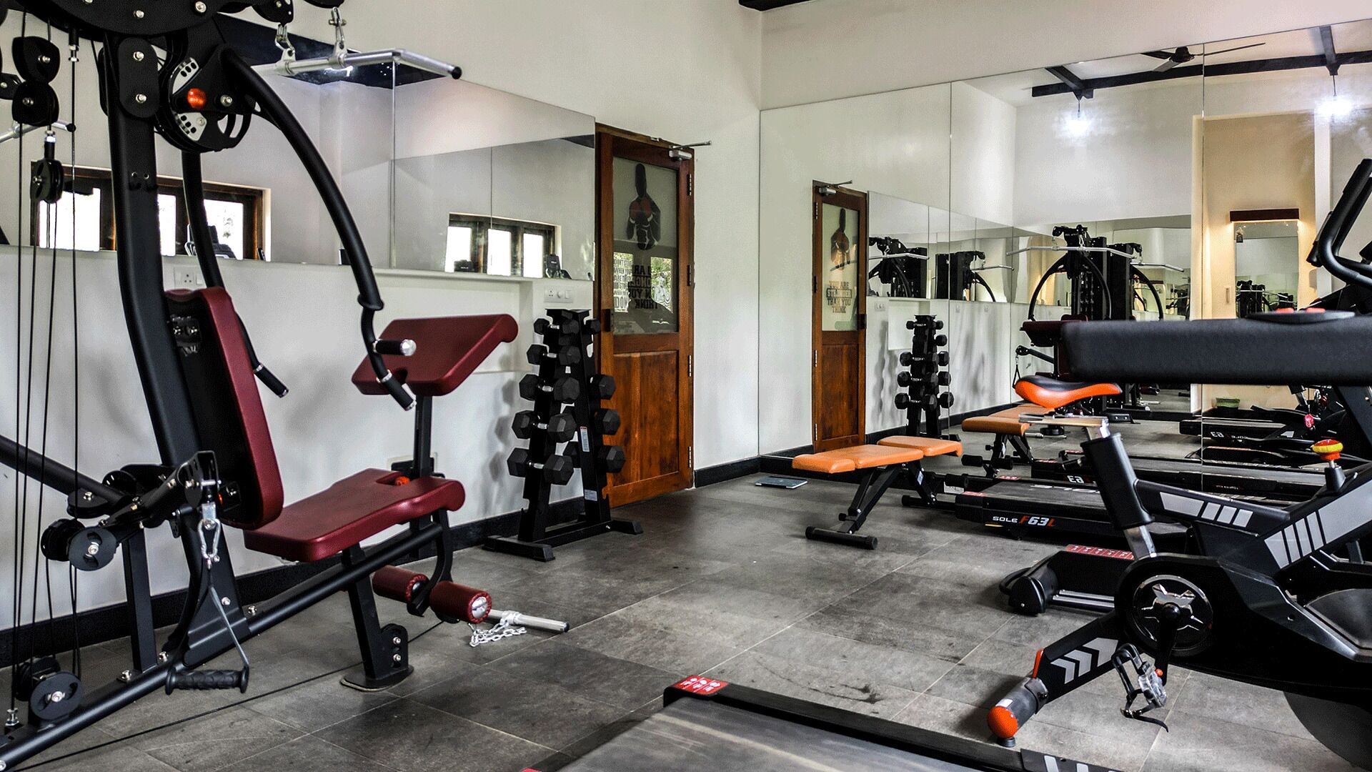 Uma academia com equipamentos de musculação, bancos e espelhos.