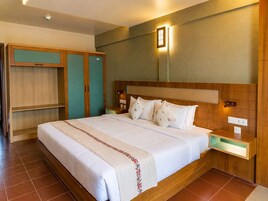 Quarto de hotel com uma cama grande, guarda-roupa de madeira e uma mesa de cabeceira.