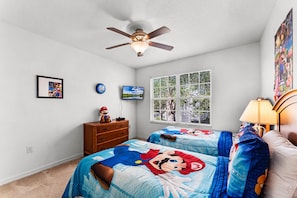 Quarto com duas camas, um ventilador de teto, TV, cômoda e janela com persianas.
