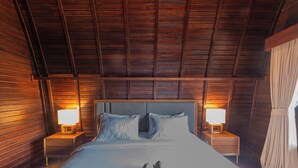 Quarto com painéis de madeira, uma cama grande, duas luminárias de cabeceira e uma cortina na janela.