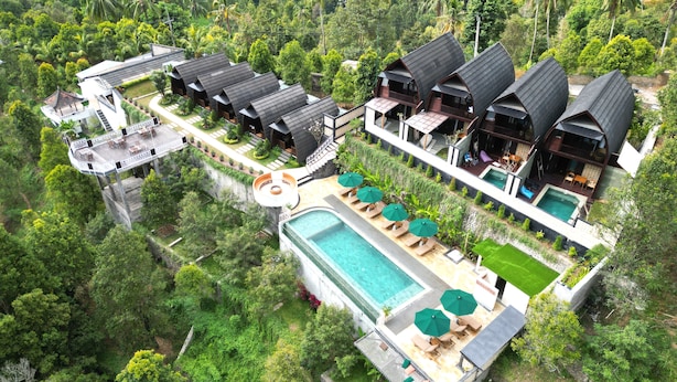 Vista aérea de um resort com várias acomodações tipo bangalô, uma piscina central e vegetação exuberante ao redor.