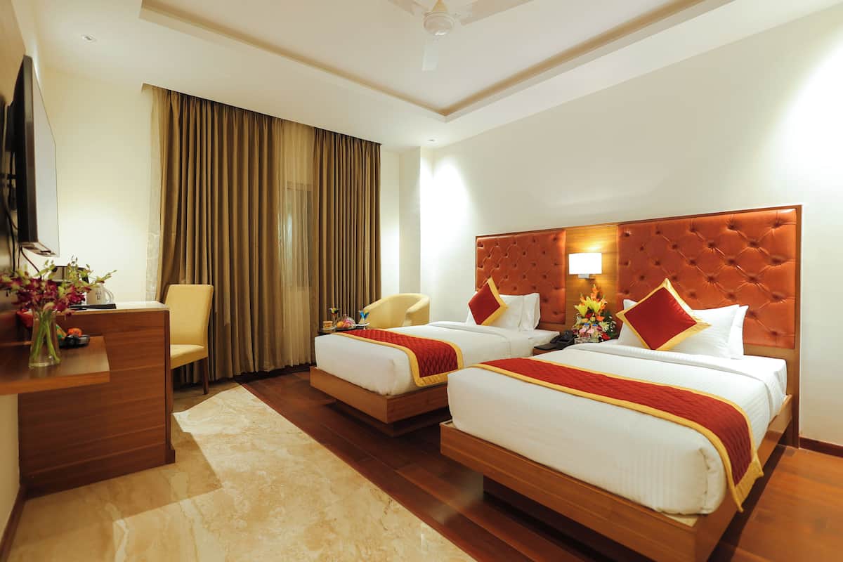 Quarto de hotel com duas camas, uma escrivaninha, uma cadeira e uma janela grande com cortinas.