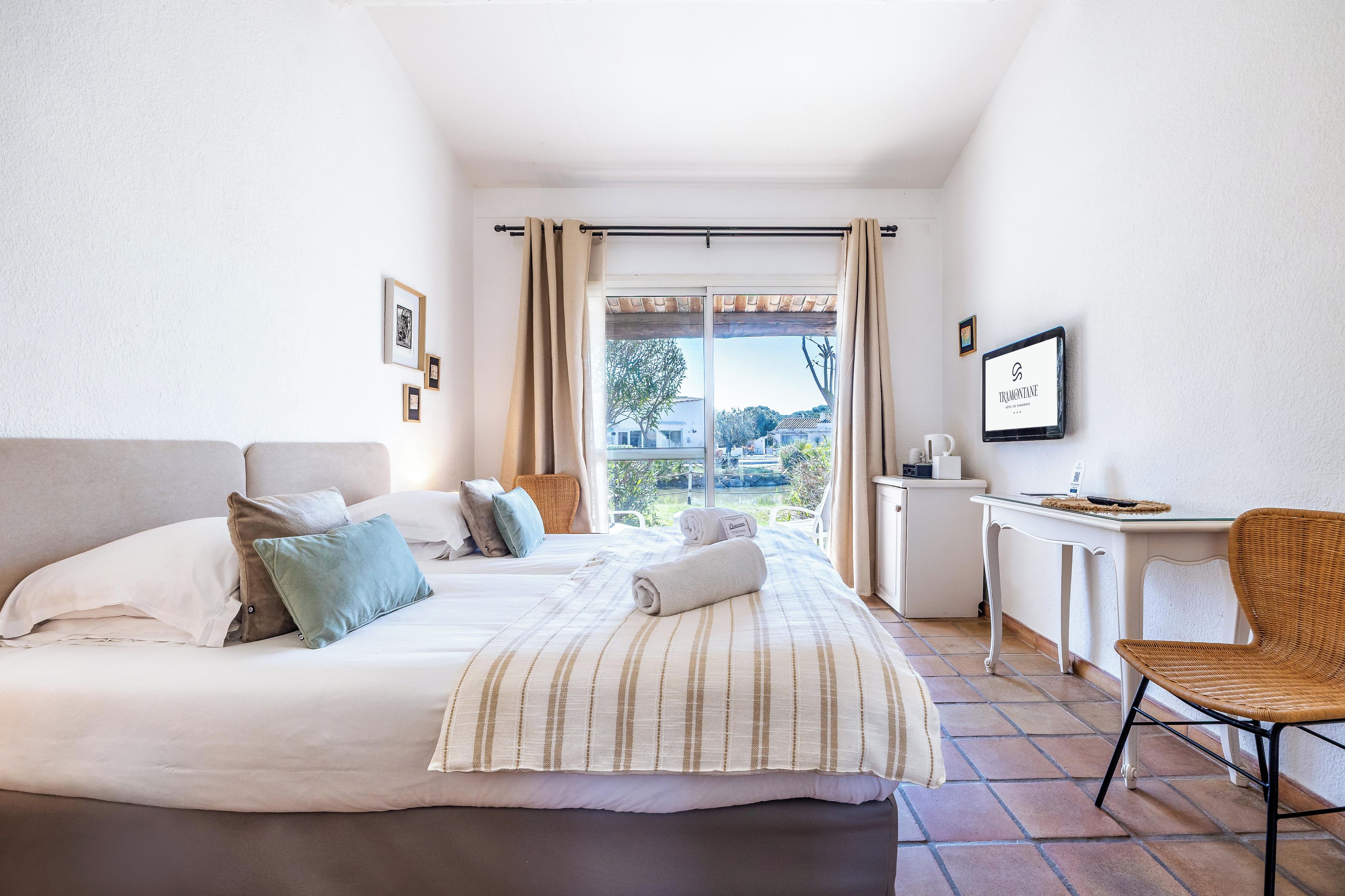 Quarto de hotel com cama, escrivaninha, cadeira e vista para o exterior.