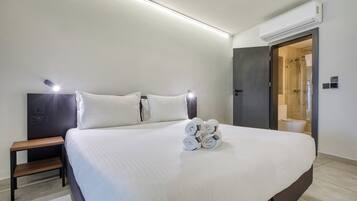 Quarto de hotel com uma cama grande, uma mesinha de cabeceira, uma escrivaninha e um aparelho de ar condicionado.