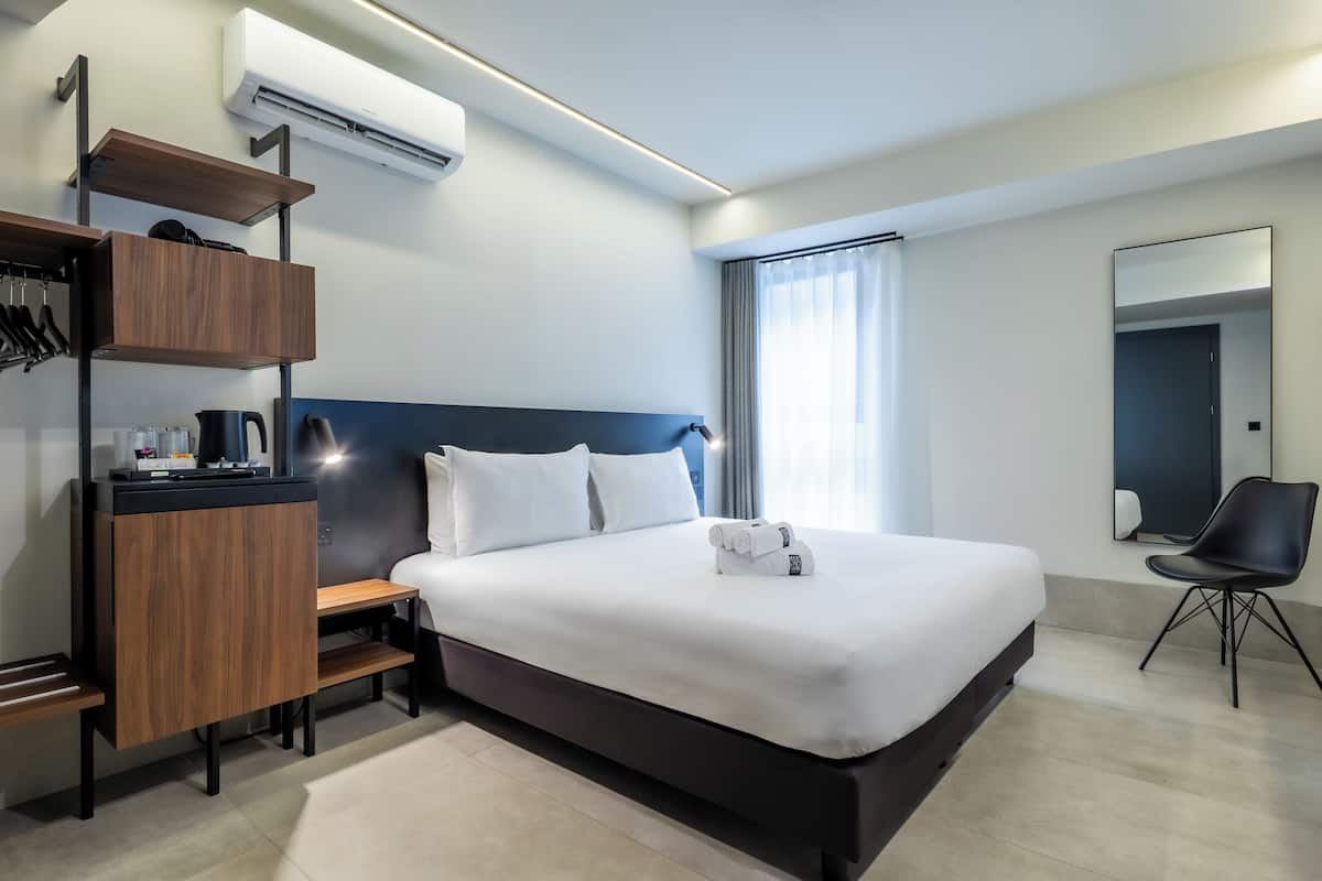 Quarto de hotel moderno com uma cama grande, um guarda-roupa de madeira, uma escrivaninha e uma cadeira.