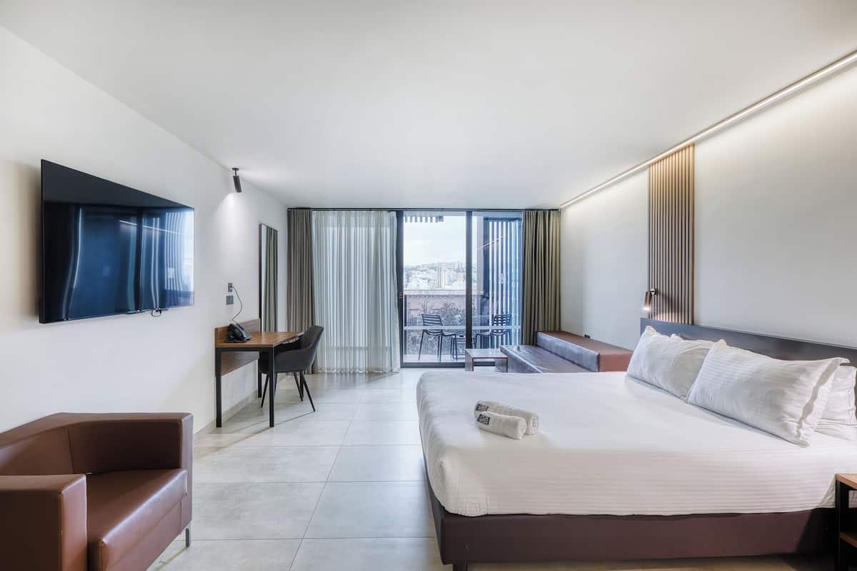 Quarto de hotel moderno com uma cama grande, uma escrivaninha e vista para a cidade.
