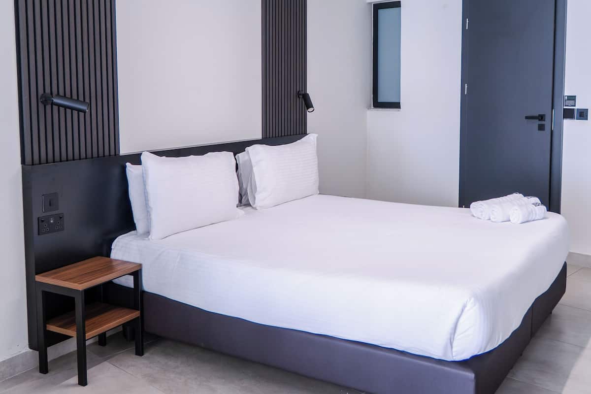 Quarto de hotel moderno com uma cama grande, mesa de cabeceira, ar condicionado fixado na parede e luminária no teto.