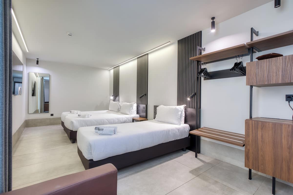 Quarto de hotel moderno com duas camas, um banco, um armário de madeira e estantes embutidas.