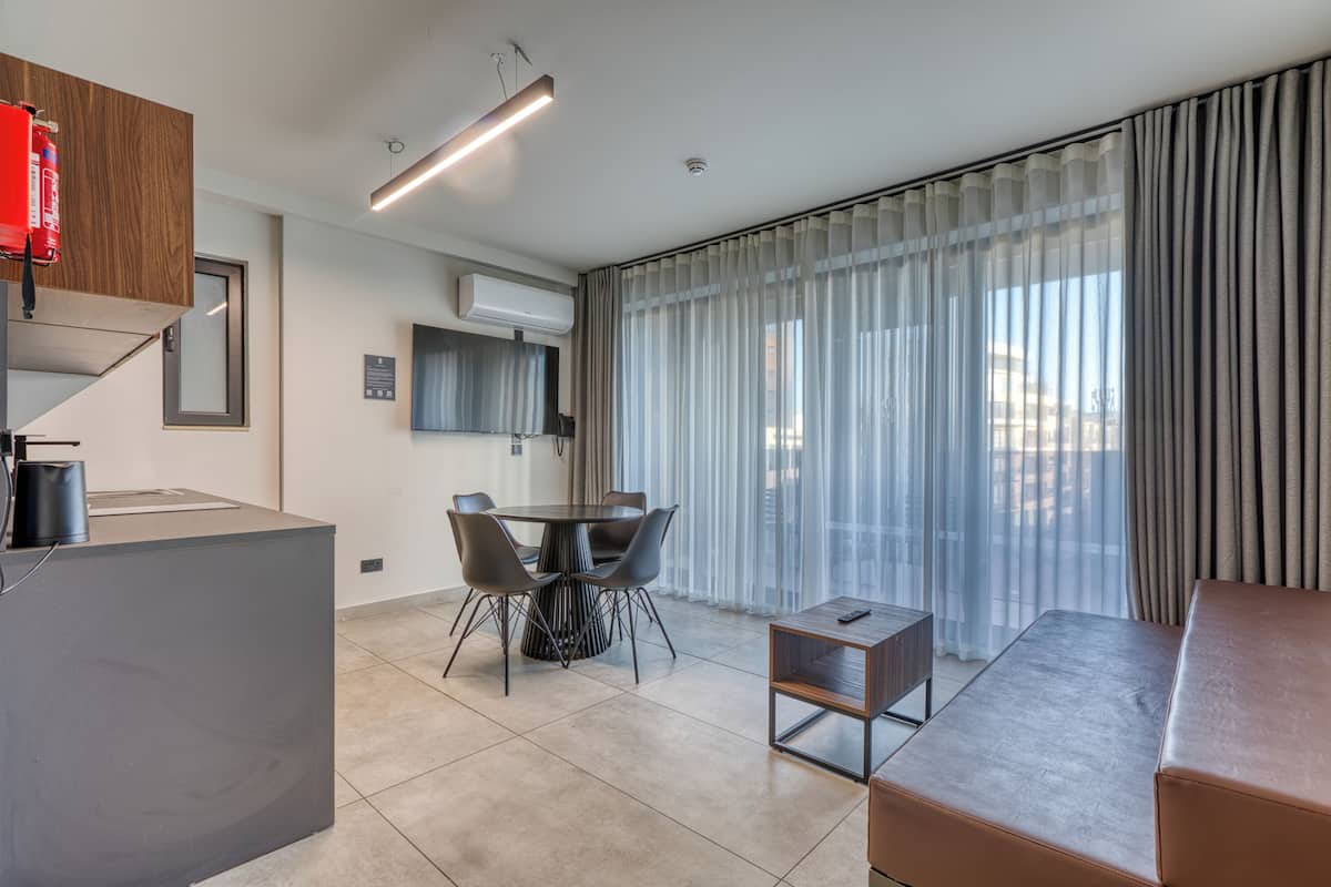 Quarto de hotel moderno com cozinha, mesa de jantar e uma grande janela com cortinas.
