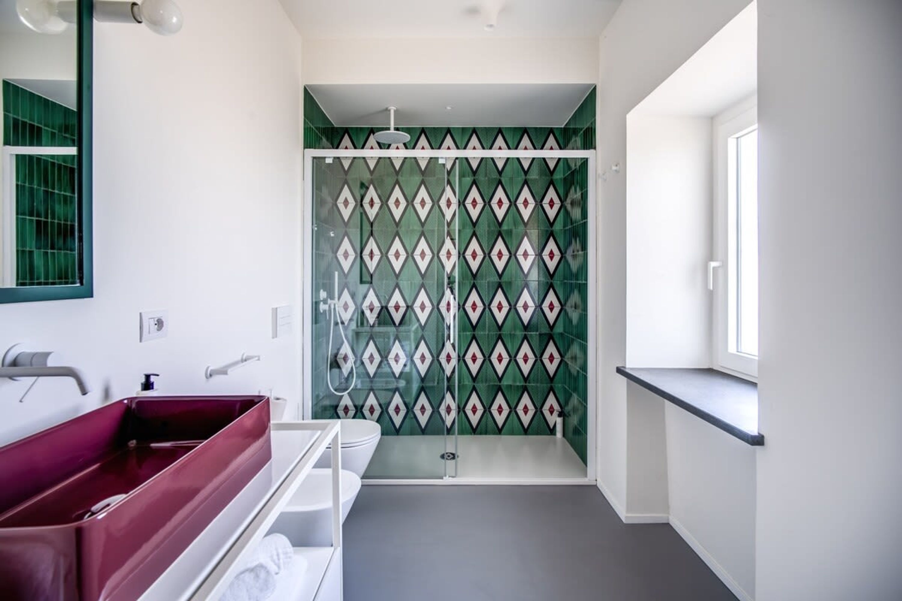 Uma casa de banho moderna com um lavatório vermelho, cabine de duche em vidro e parede com padrão verde.