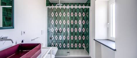 Uma casa de banho moderna com um lavatório vermelho, cabine de duche em vidro e parede com padrão verde.