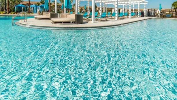 Uma área de piscina com espaço de estar coberto, espreguiçadeiras e guarda-sóis.