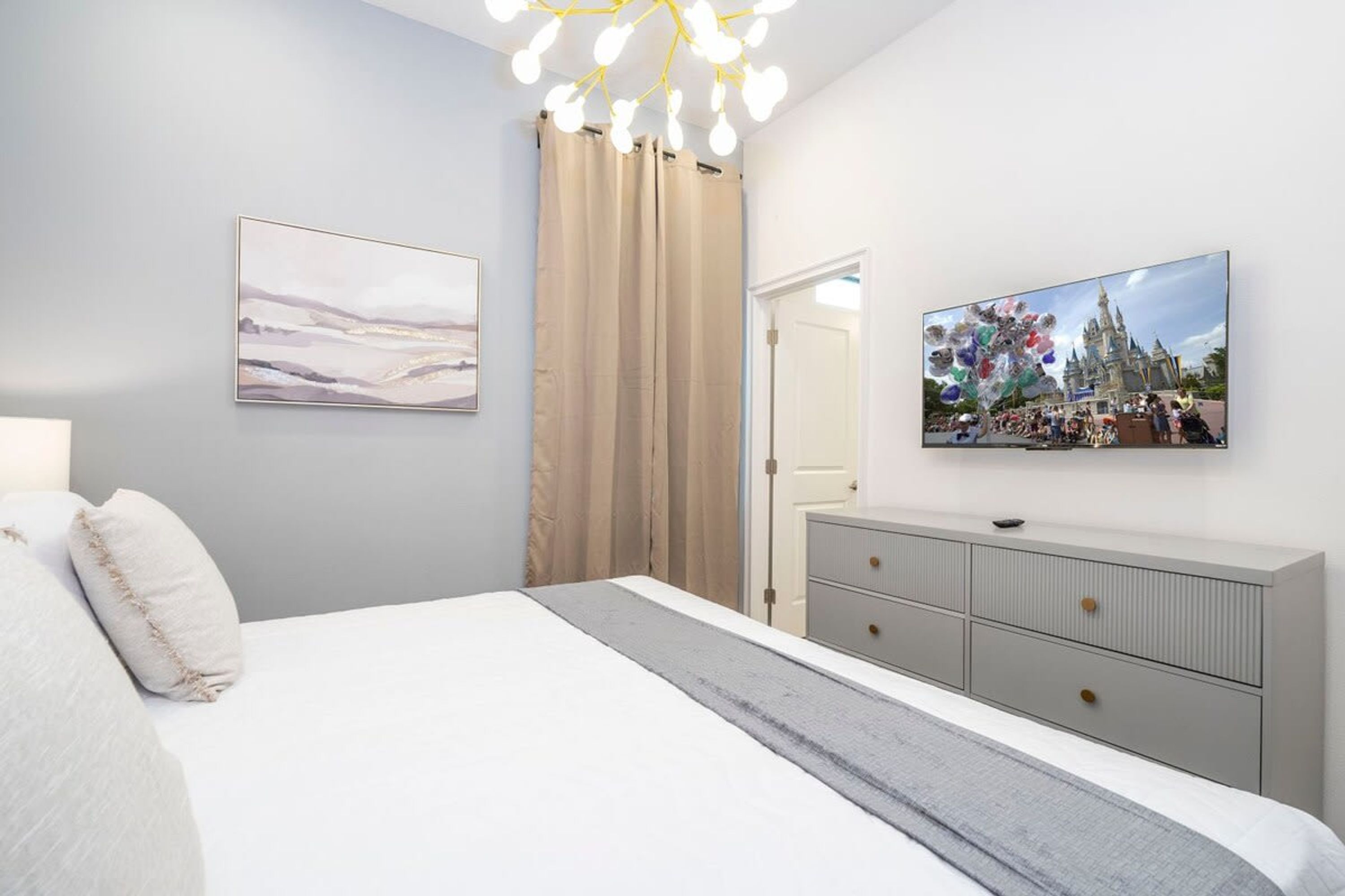Quarto moderno com cama grande, televisão de tela plana, cômoda e janela com cortinas.