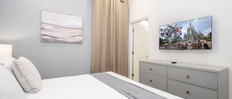 Quarto moderno com cama grande, televisão de tela plana, cômoda e janela com cortinas.