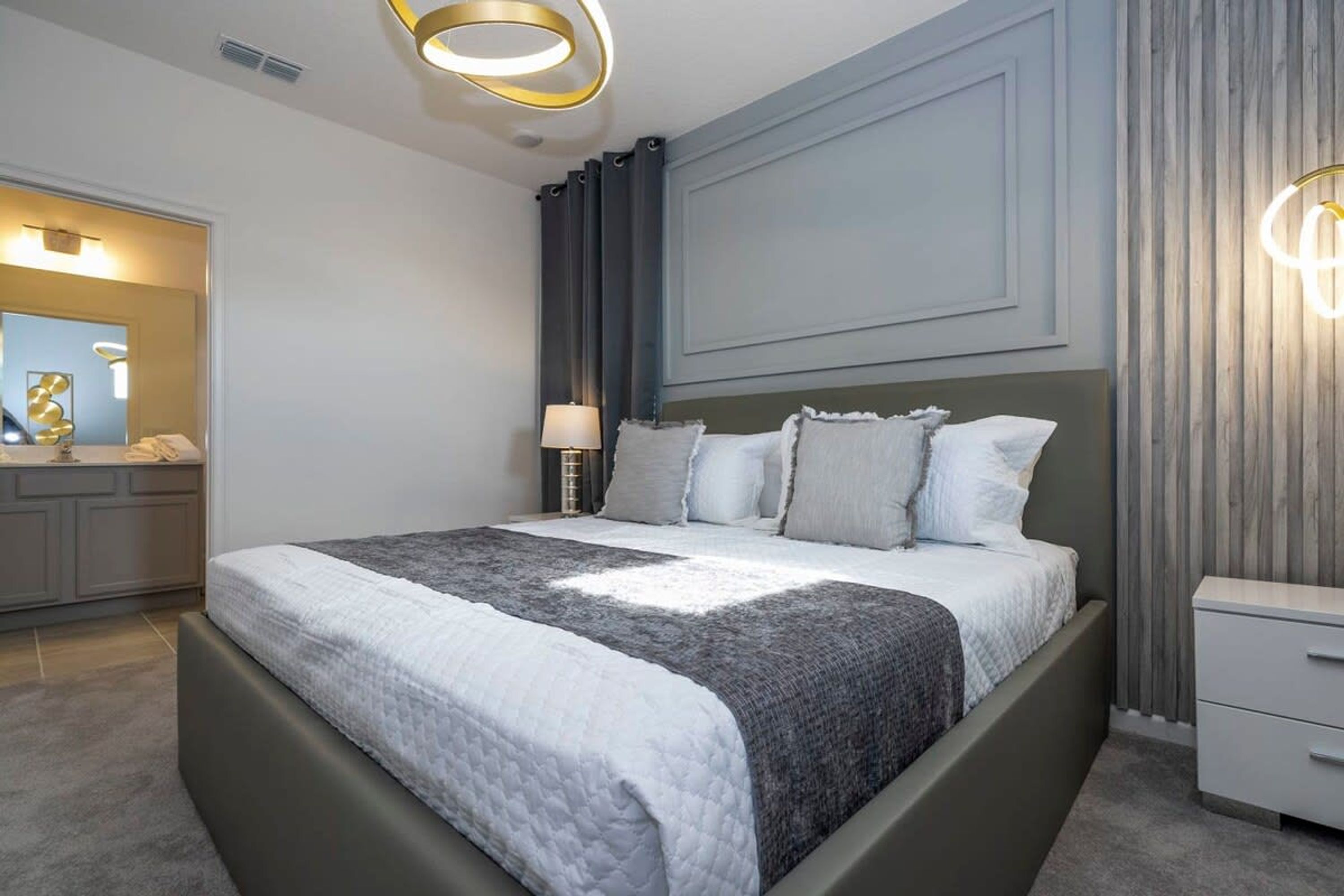 Quarto moderno com uma cama grande, mesa de cabeceira, espelho e luminária fixa na parede.