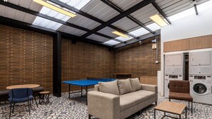 Quarto com mesa de pingue-pongue, sofá, máquina de lavar e piso estampado.
