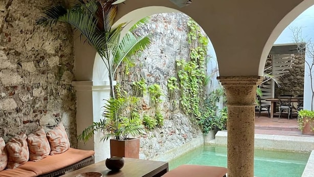 Uma área de estar aconchegante com parede de pedra, ventilador de teto e vista para uma piscina.