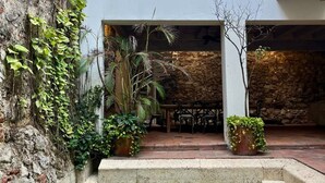 Um pátio com piscina, paredes de pedra, venezianas de madeira e plantas em vasos.