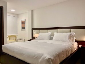 Cama bem arrumada com lençóis brancos, cabeceira de madeira e mesa de cabeceira com abajur.