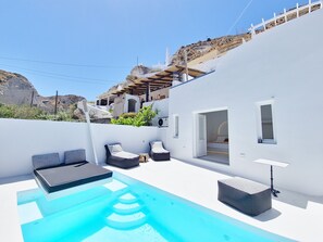 Uma área moderna com piscina ao ar livre, água azul cristalina, espreguiçadeiras e um edifício branco com vista para a paisagem circundante.