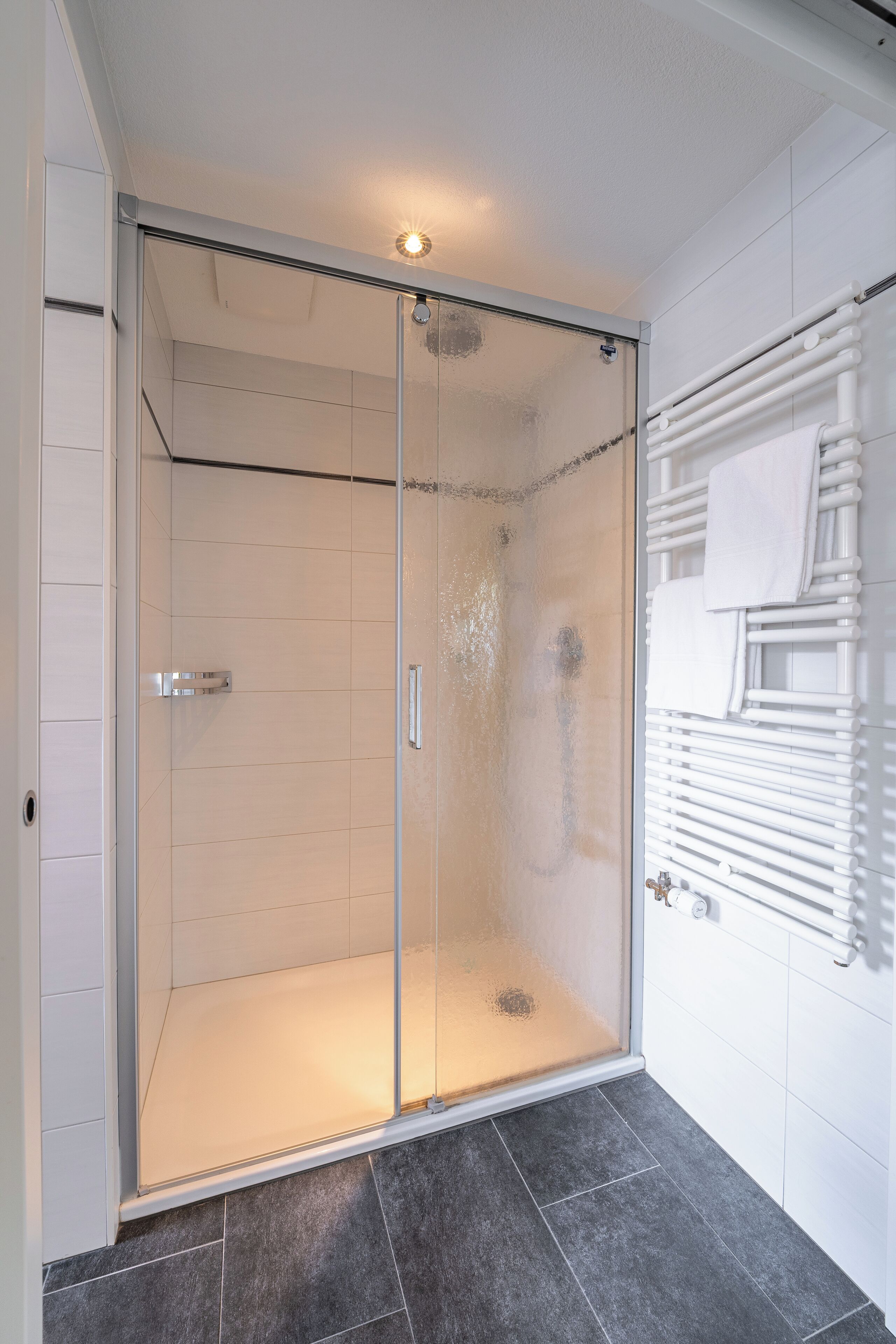 Um box de chuveiro moderno com porta de vidro, porta-toalhas branco e piso revestido de azulejos.