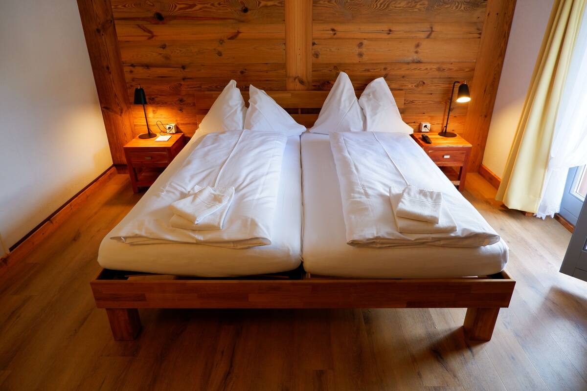 Uma cama de casal com lençóis brancos, duas mesas de cabeceira com abajures e paredes de madeira.