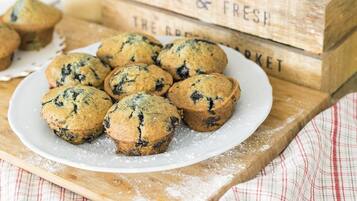 Um prato de muffins de blueberry sobre um prato branco, com uma caixa de madeira com a etiqueta 'LOCAL & FRESH' ao fundo.