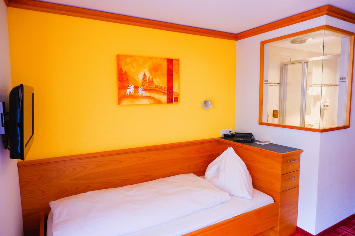 Quarto de hotel com cama de madeira, pintura de uma cena florestal, espelho e cômoda de madeira.