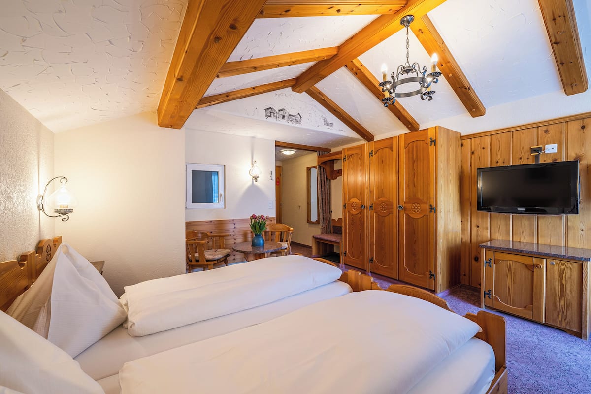 Quarto de hotel com vigas de madeira, uma cama, uma televisão e um guarda-roupa de madeira.