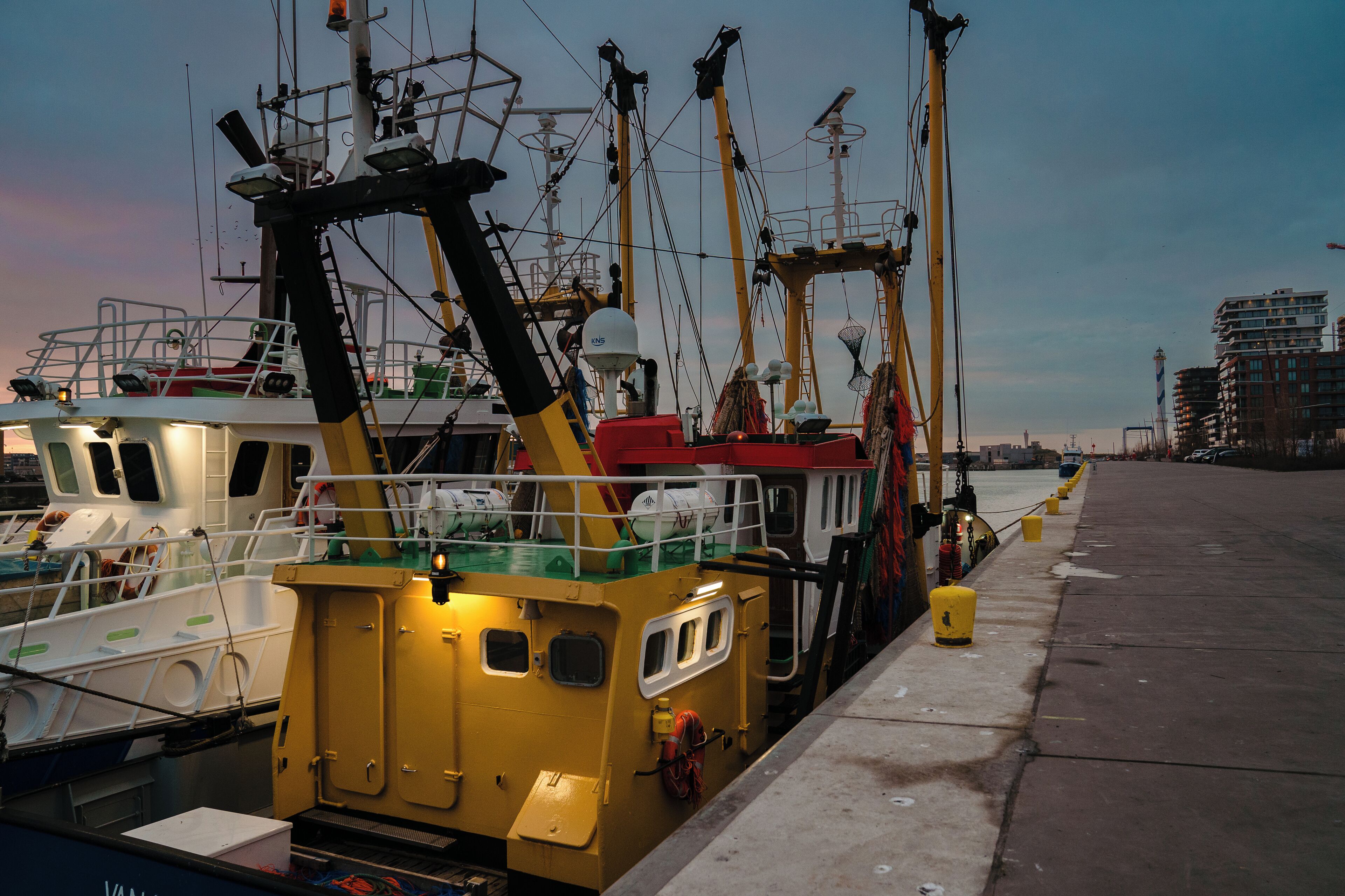 Uma marina com vários barcos atracados, incluindo uma embarcação amarela e branca com cabine e um barco vermelho e branco também com cabine.