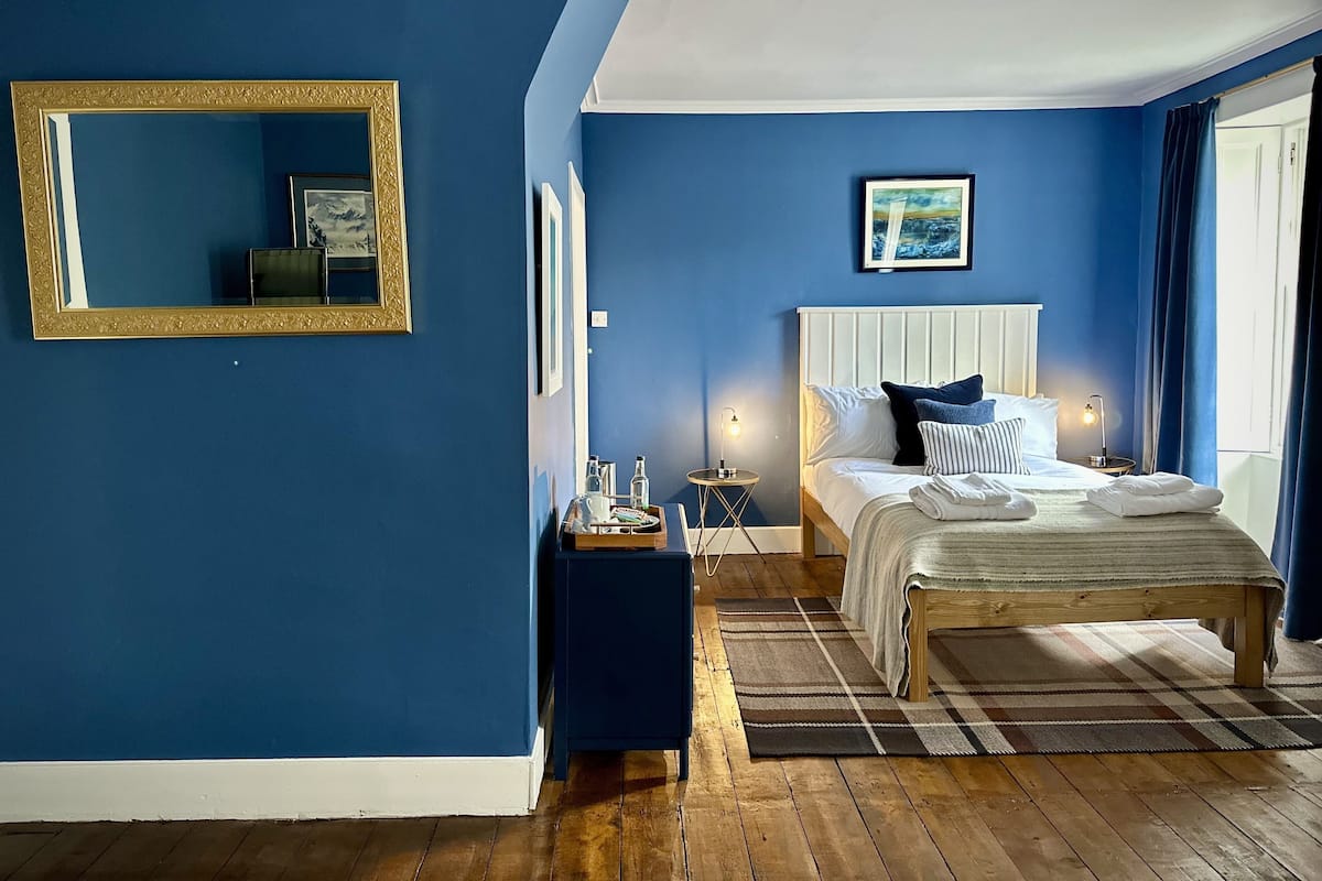 Quarto com cama, mesas de cabeceira, espelho e obras de arte nas paredes.