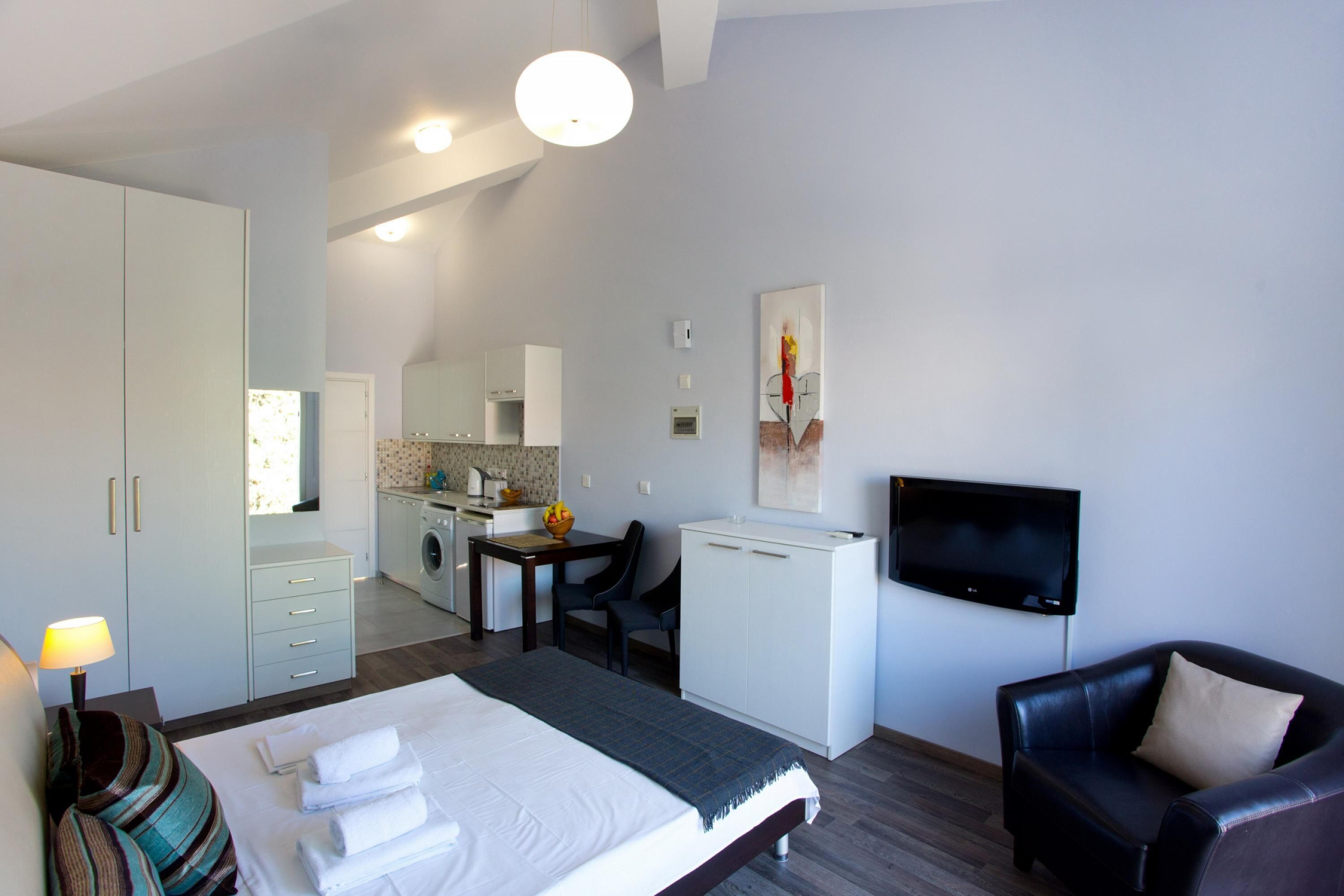 Quarto de hotel moderno com cama, escrivaninha, cadeira, televisão e guarda-roupa.