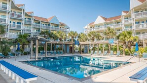 Um hotel com piscina, várias varandas e palmeiras.