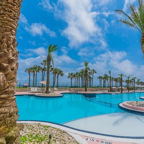 Uma área de piscina com várias piscinas, palmeiras e céu azul límpido.