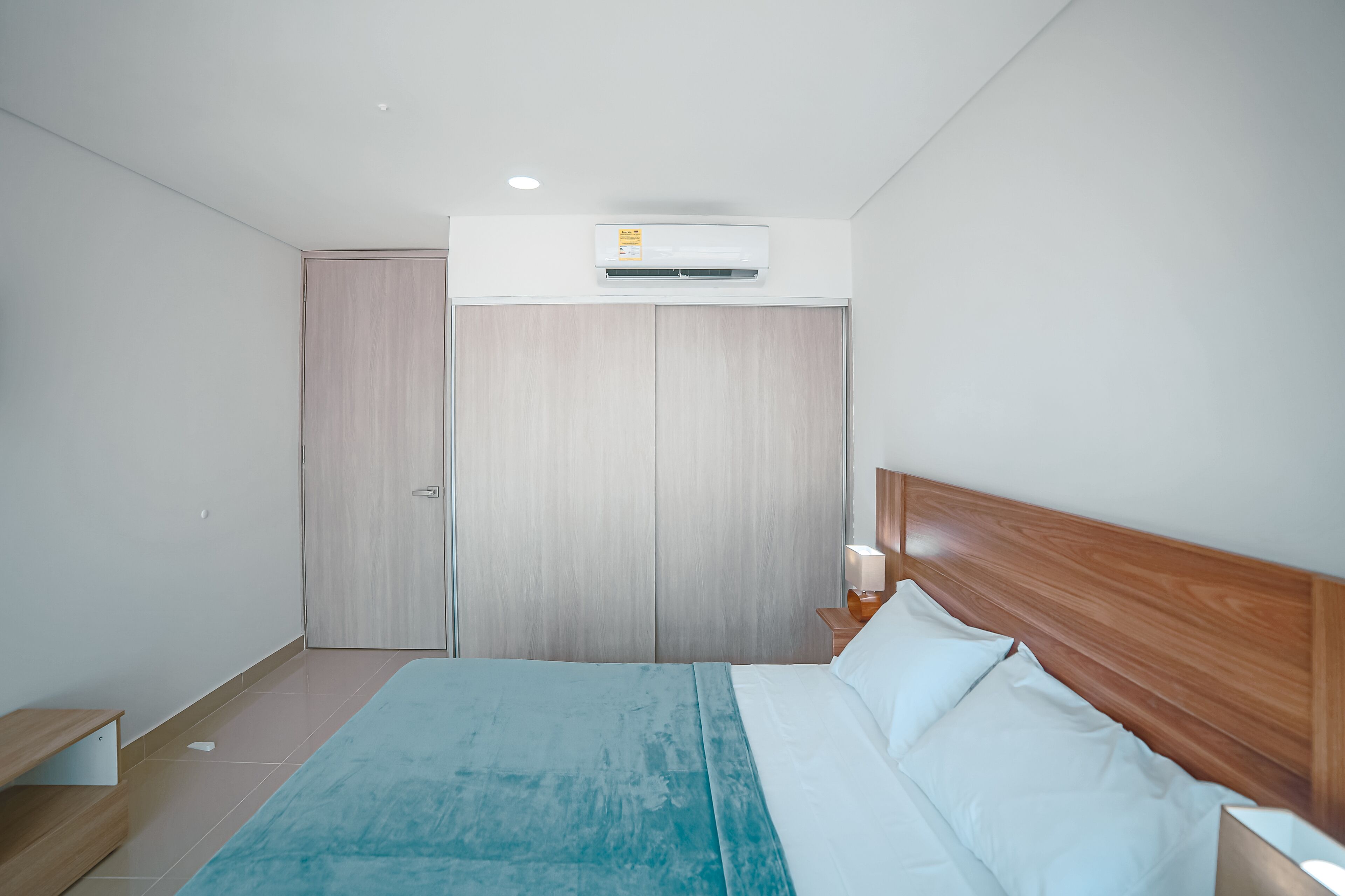 Um quarto com cama, mesa de cabeceira, cabeceira de madeira, guarda-roupa e ar condicionado.