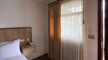 Quarto de hotel com cama, mesa de cabeceira e janela com cortinas.
