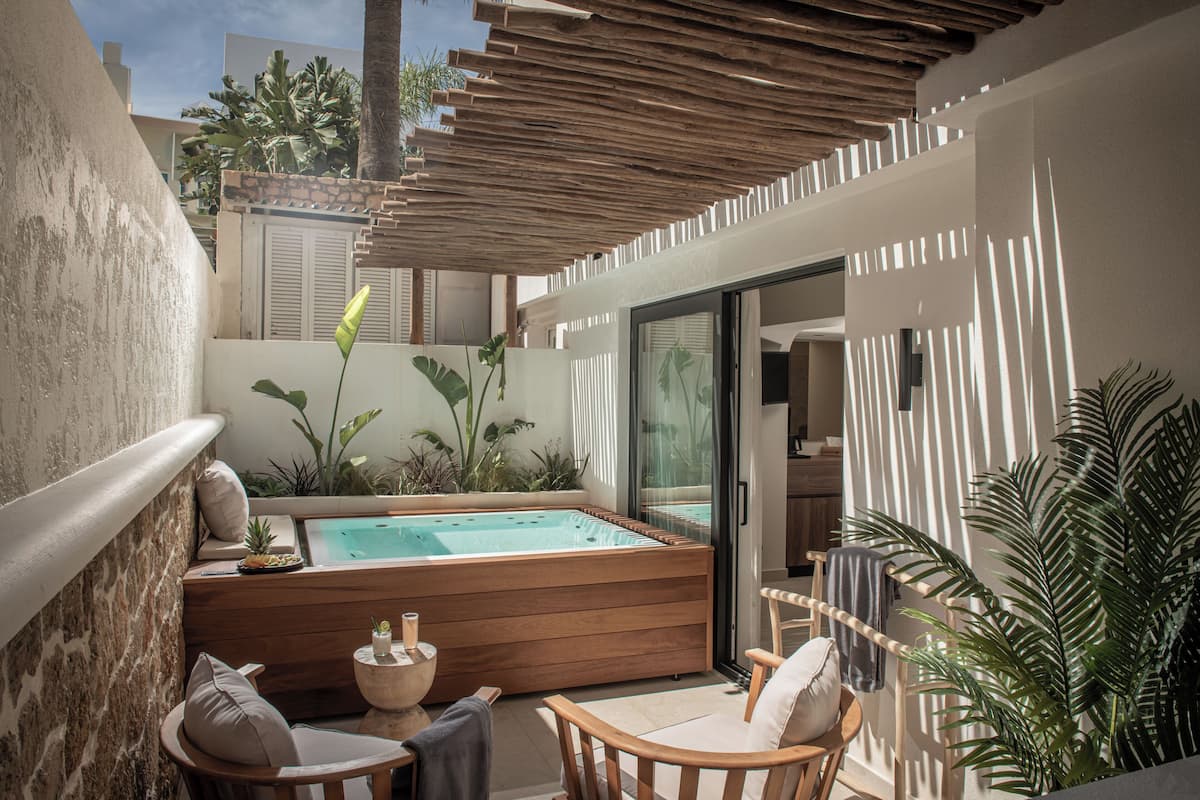 Área de spa com hidromassagem, assentos de madeira e plantas tropicais.