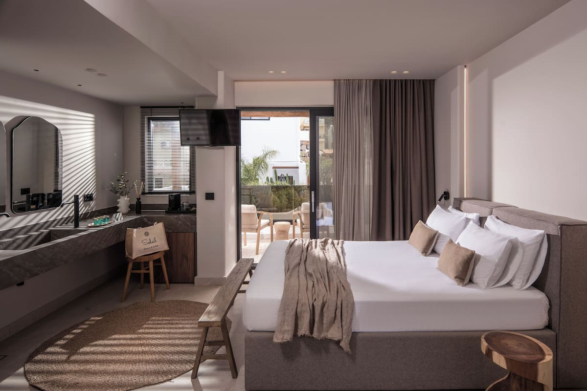 Quarto de hotel moderno com uma cama grande, uma escrivaninha e varanda com área de estar.