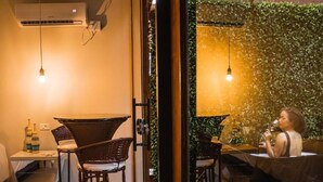 Um ambiente acolhedor com área de jantar, cadeiras de vime e uma mesa, área de bar com banquetas e uma parede decorada com plantas.