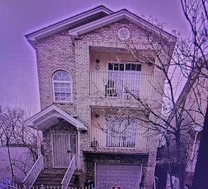 Uma casa de dois andares com varanda frontal, garagem e placa de 'Proibido Estacionar'.