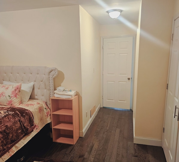 Um quarto com uma cama, uma estante de madeira, uma porta e um corredor.