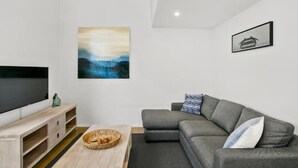 Uma sala de estar moderna com um sofá seccional cinza, uma TV de tela plana, uma mesa de centro de madeira e uma pintura na parede.