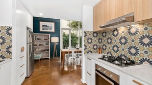 Cozinha moderna com armários brancos, geladeira de aço inoxidável, fogão a gás e painel de fundo decorado.